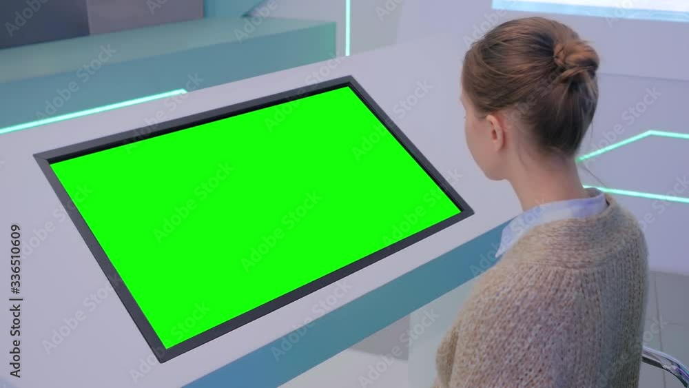 Woman looking at blank digital interactive green display kiosk at ...