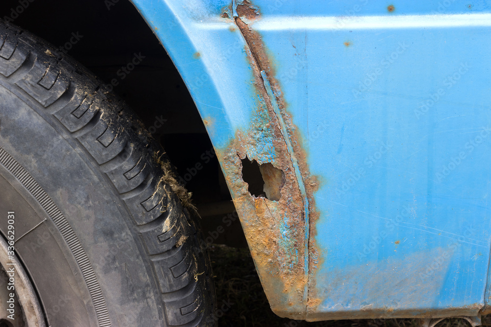 The old battered car is blue, with traces of rust and damage. It is ...