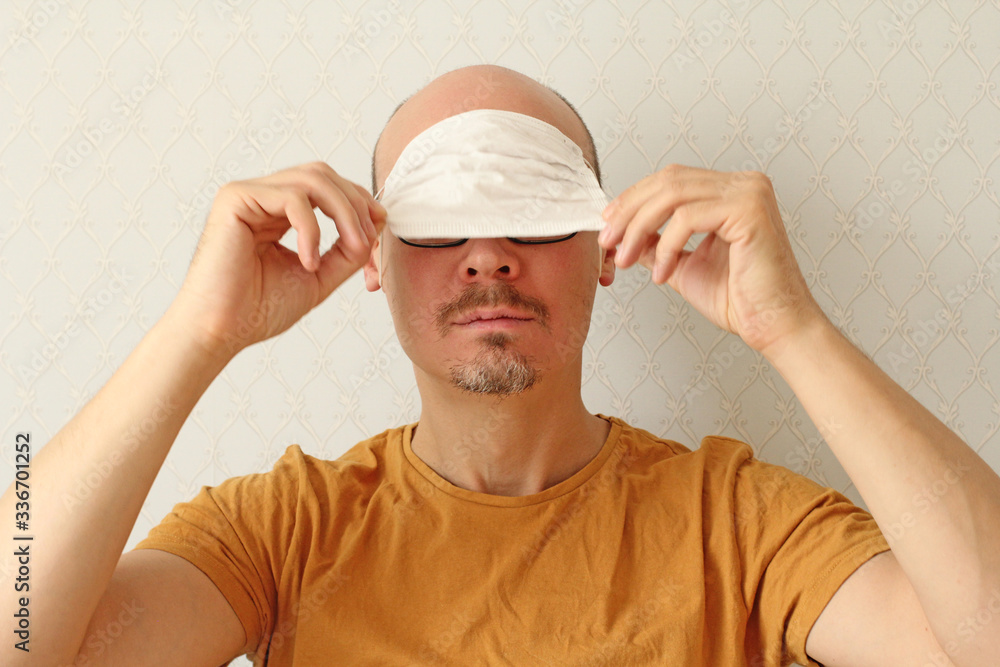 Young man incorrectly puts disposable protective white medical hygiene ...