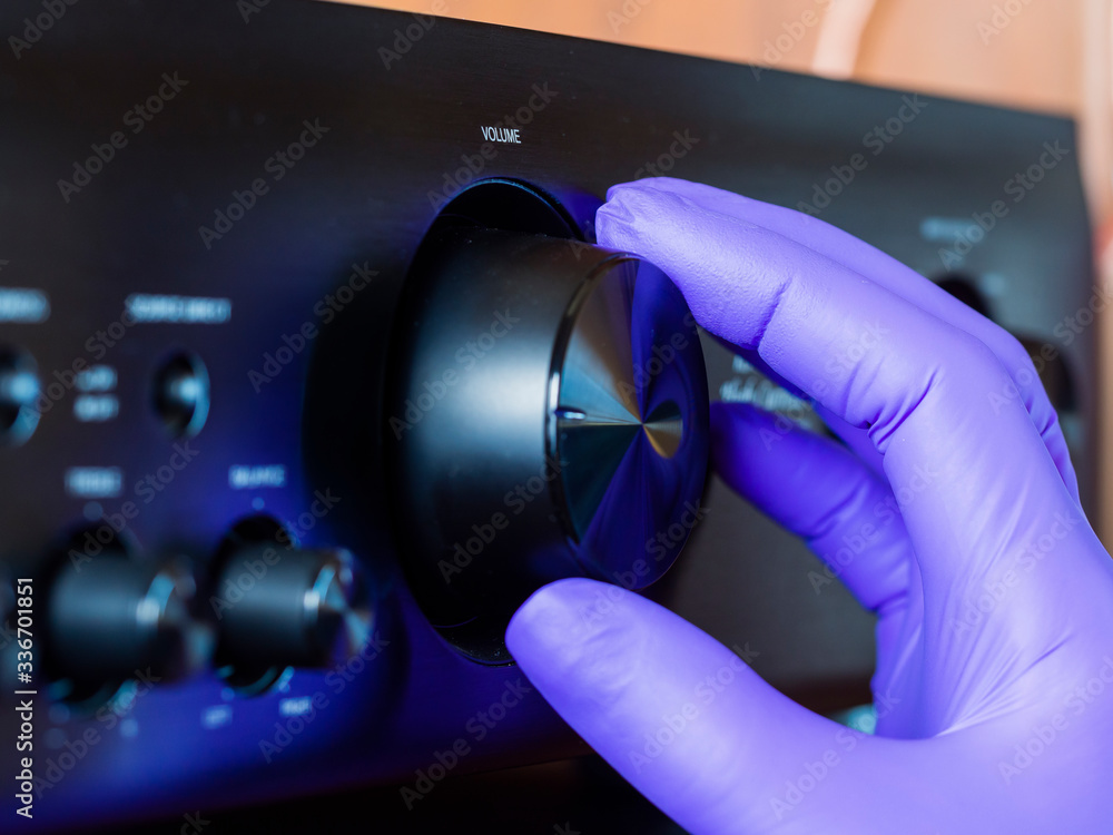 Purple medical-gloved hand controls the volume of a hifi amplifier ...
