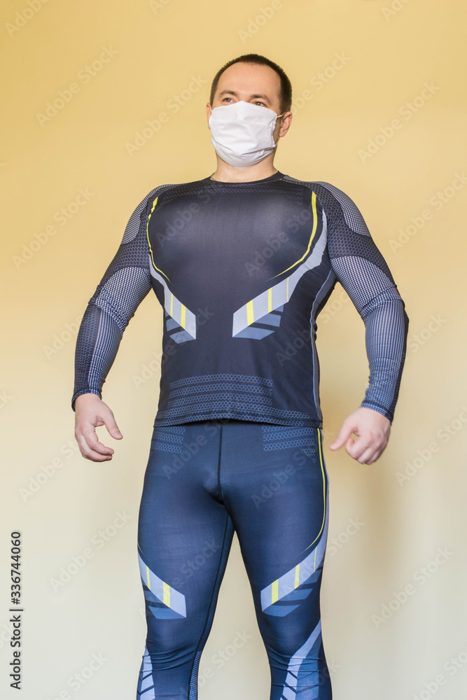 Strong young man in an elastic suit for fitness and a mask on his face ...