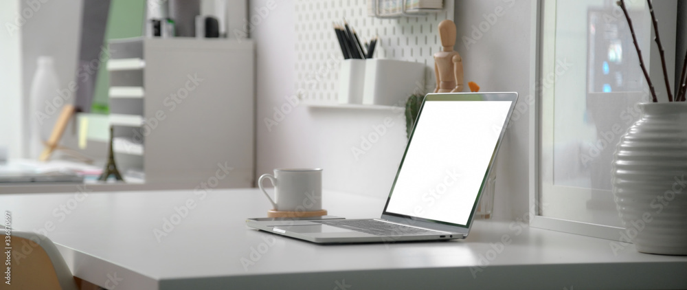 Side view of minimal office desk with blank screen laptop, coffee cup ...