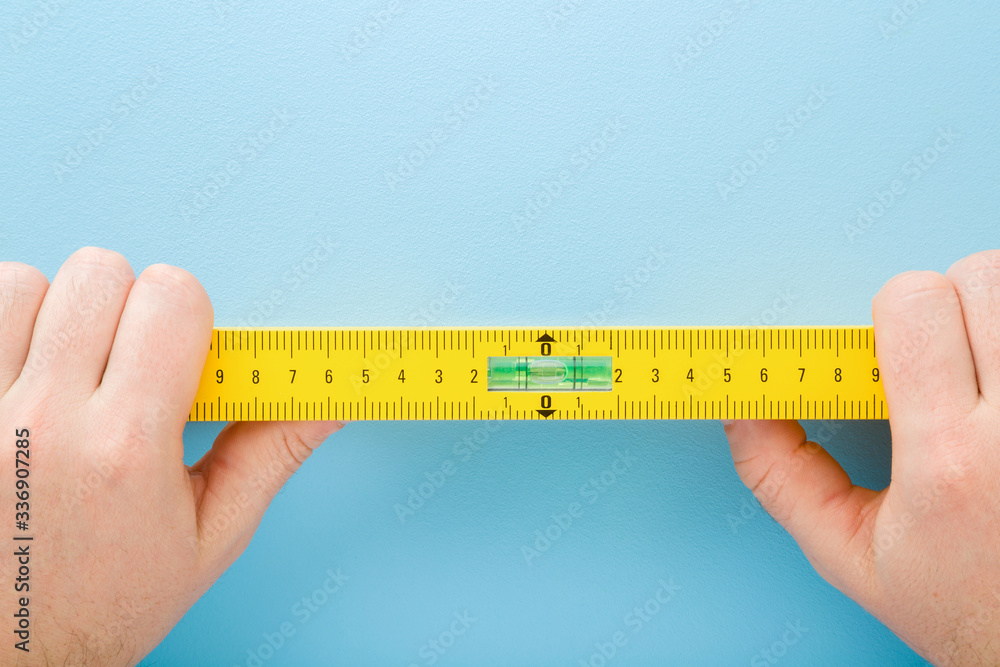 Man hands holding yellow spirit level with measuring scale. Blue table ...