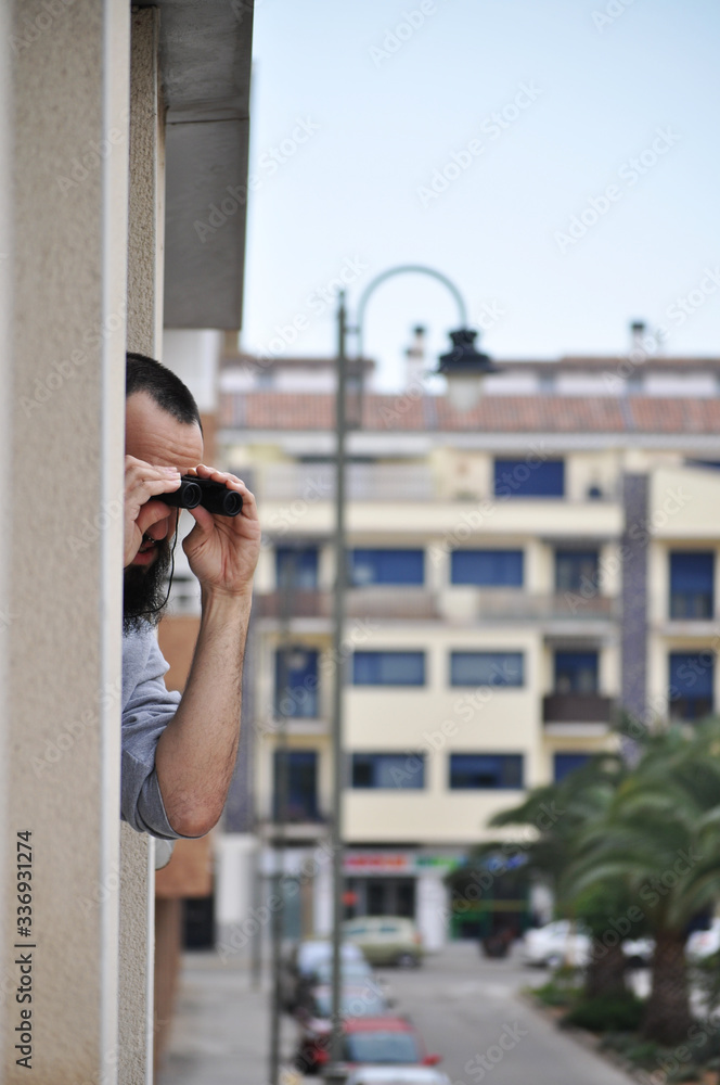 Young man leaning out of apartment window looking through binoculars in ...