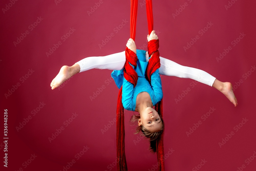 Little acrobat girl doing splits in the air holding on to a red air ...