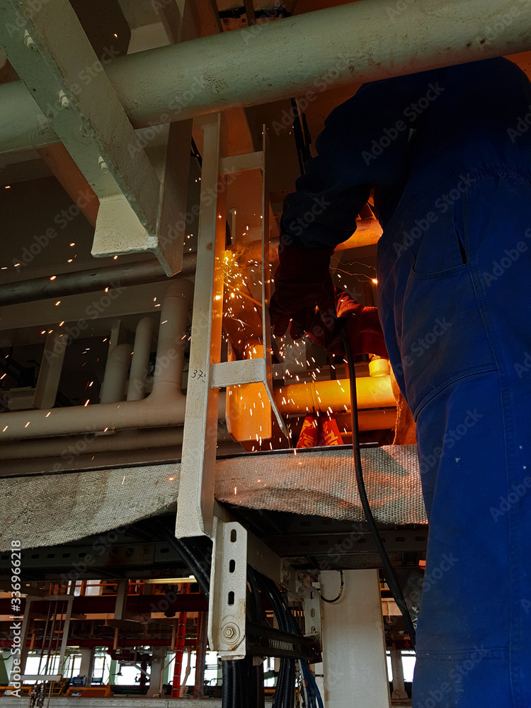 Welder welding steel angle bars for piping installation onboard a ship ...