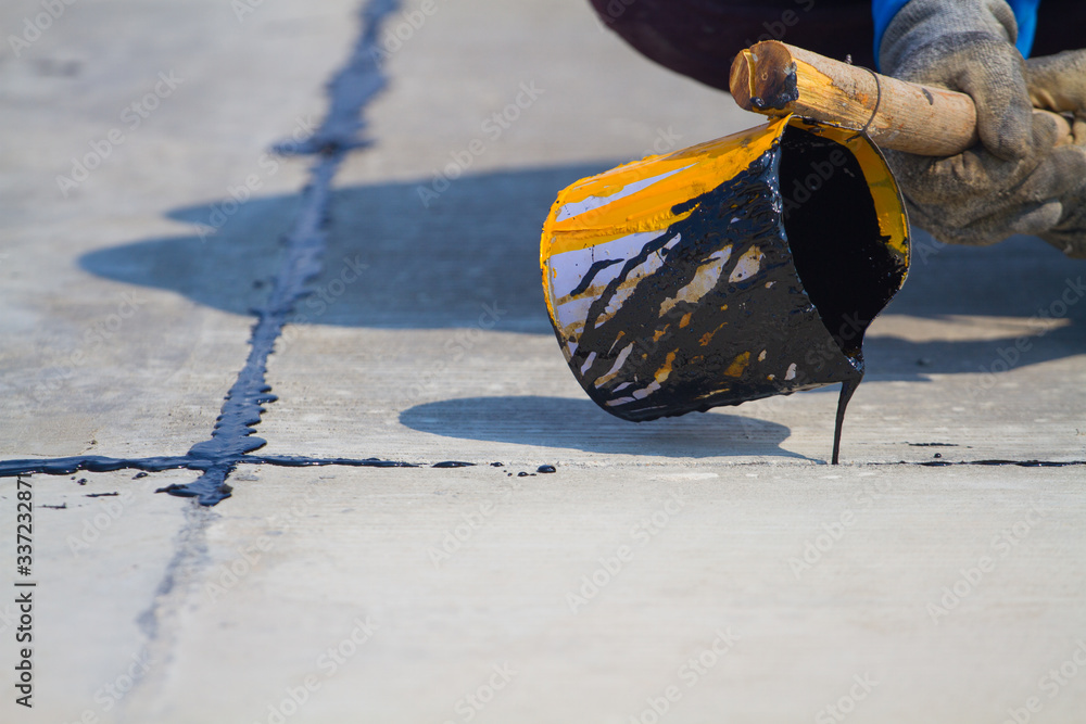Worker sealing asphaltic joint for construction joint on concrete ...