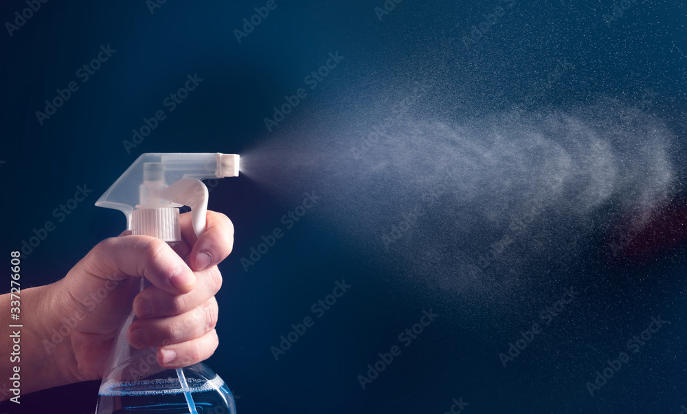 On a dark background, a Hand with a spray bottle. A spray of water ...