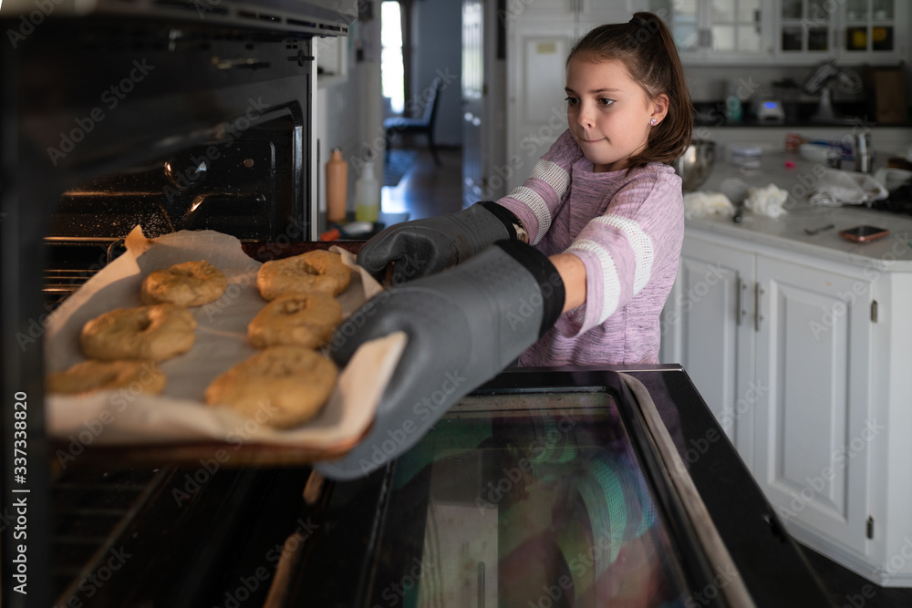 Teenage girl wearing oven mitts pulling bagels out of the oven Stock ...