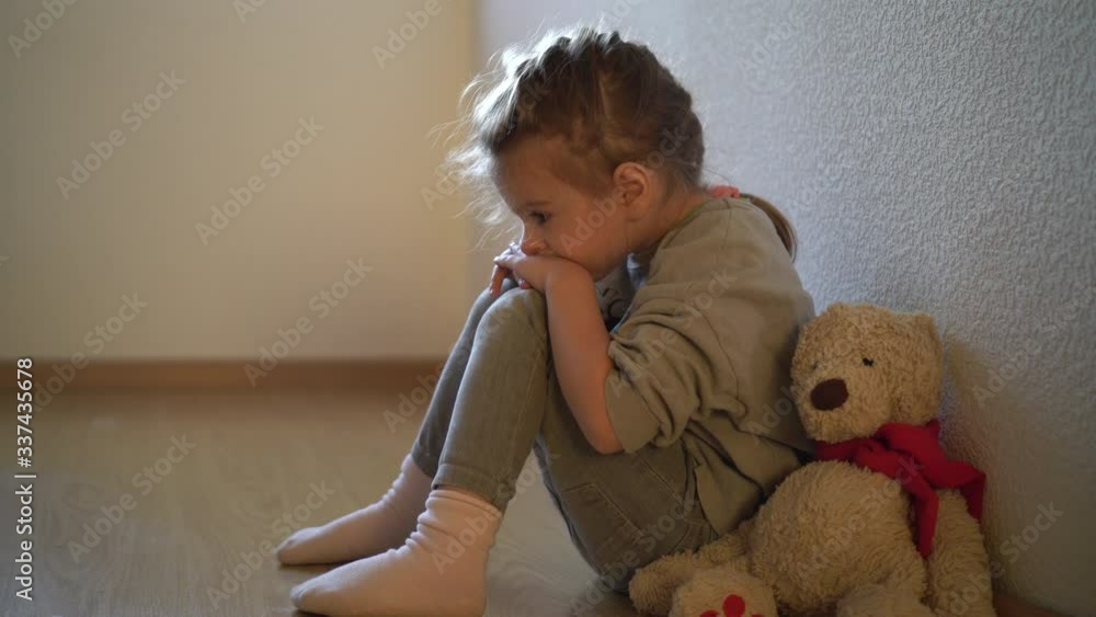 Abandoned child. Little girl beside the wall by the window alone with ...