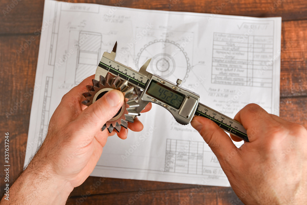 A working engineer checks the size of a bevel gear with an electronic ...