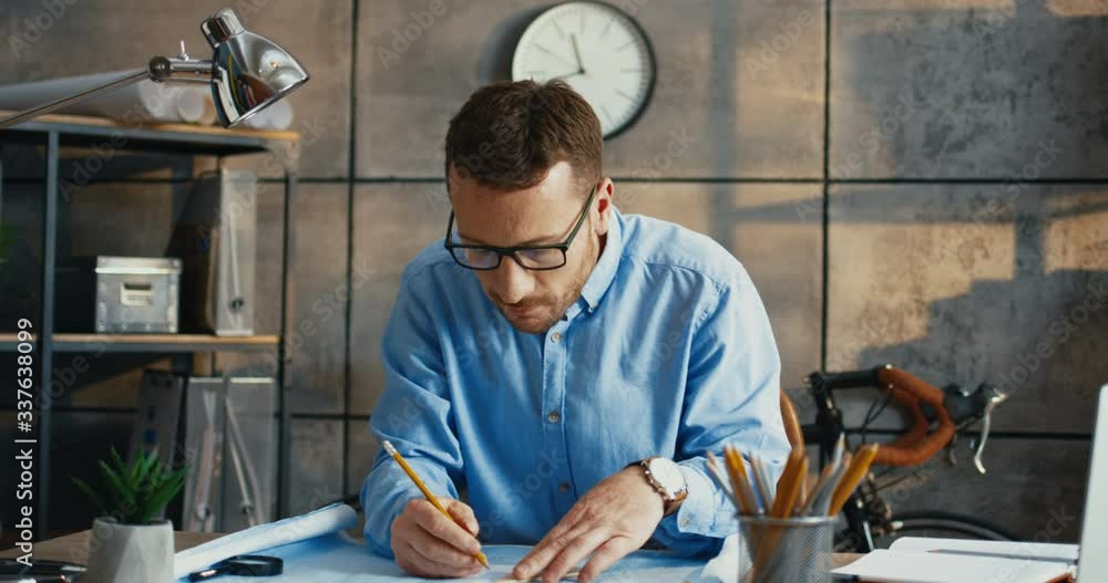 Portrait of serious male professional drawing with pencils plan while ...
