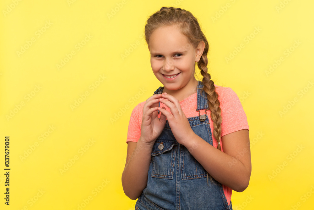 Portrait of sneaky scheming little girl in denim overalls thinking over ...