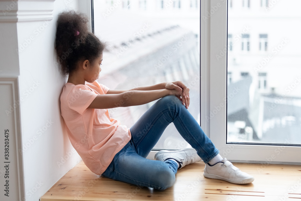 Pensive african american young girl sitting alone on windowsill in ...