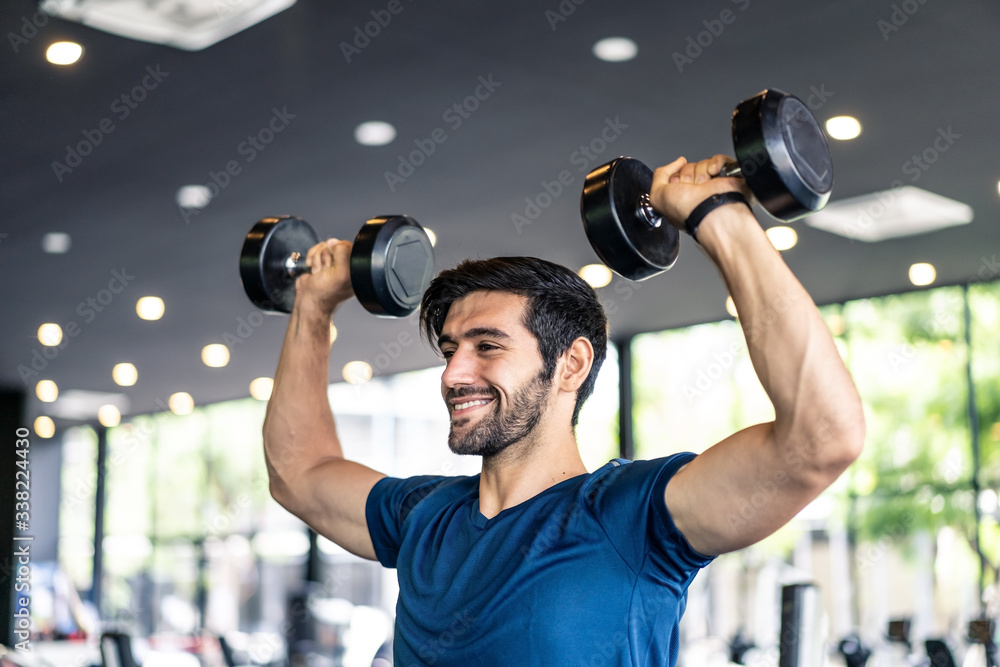 Young fit Caucasian handsome man lifting weights dumbbell both hands in ...