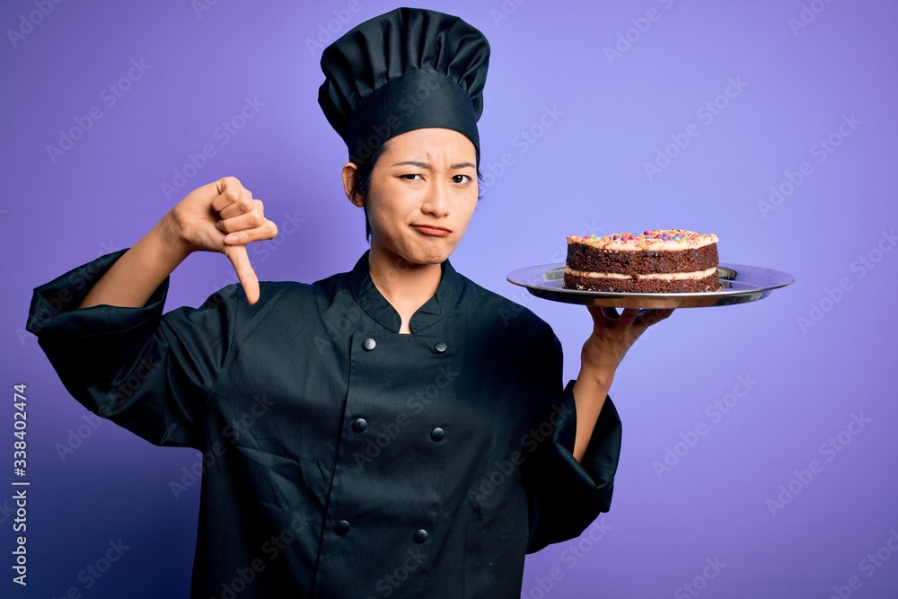 Foto de Young chinese chef woman wearing cooker uniform and hat holding ...