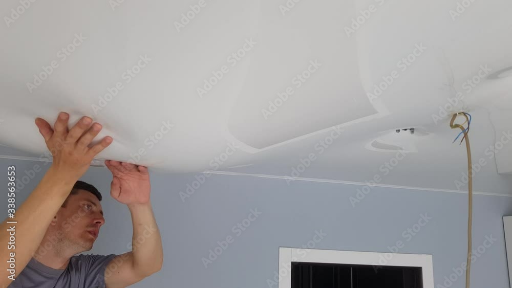 Men is drain water from a stretch ceiling filled with water through a ...