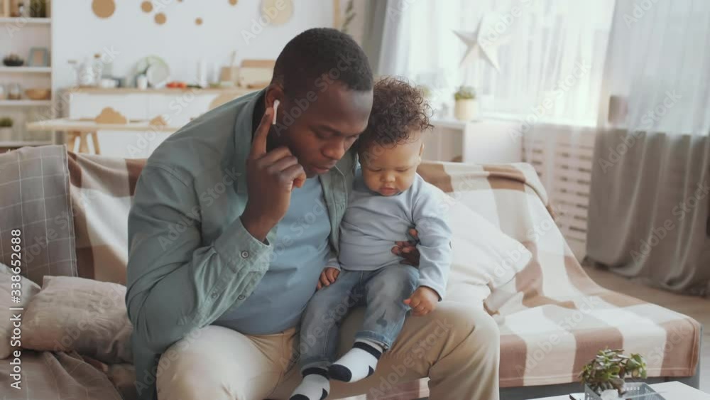 African man sitting on couch in living room with little curly-haired ...
