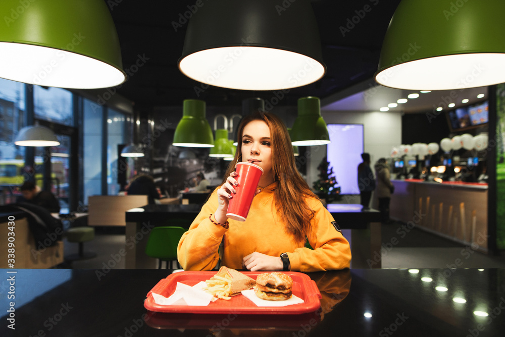 Foto de Attractive girl sits with a tray of fast food in a cafe and ...