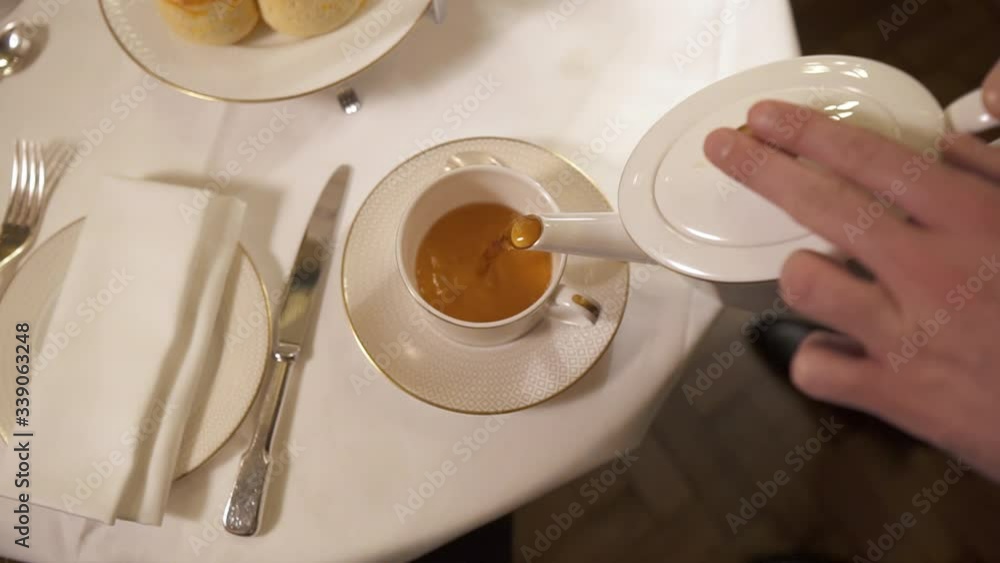 A waiter is serving a perfectly brewed black tea at the table while the ...
