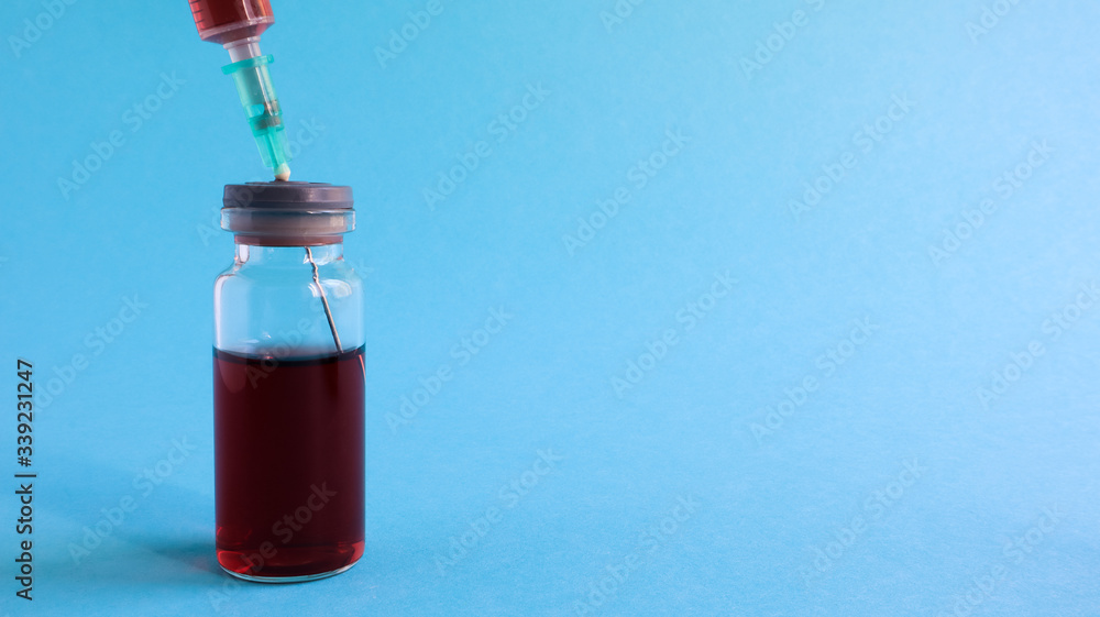 A syringe sticks out of a red liquid bottle. Isolated on a blue background. Medicine, injections ...
