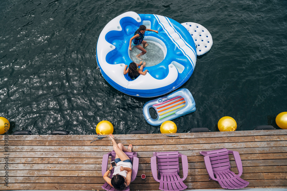 Girls jumping on giant floaty on lake while mom watches from dock Stock ...