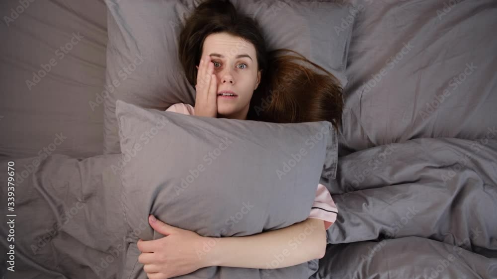 Top view of scared young woman lying in grey bed look at camera feel ...