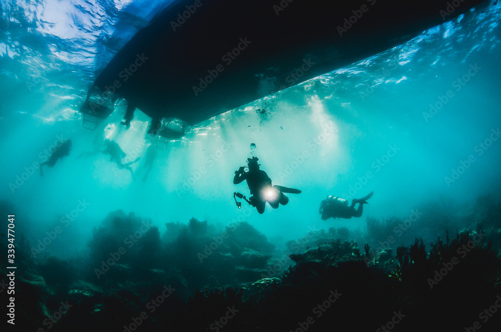 Underwater silhouette shot of scuba divers and a dive boat with golden ...