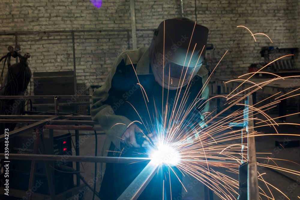 Welder welding a metal part in an industrial environment, wearing ...