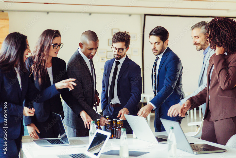 Relaxed office managers taking beer bottles from table. Cheerful young ...