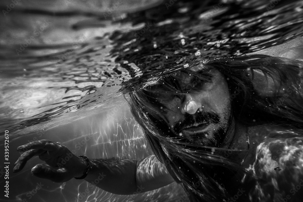 Artistic pic out of focus underwater with long hair man swimming with ...