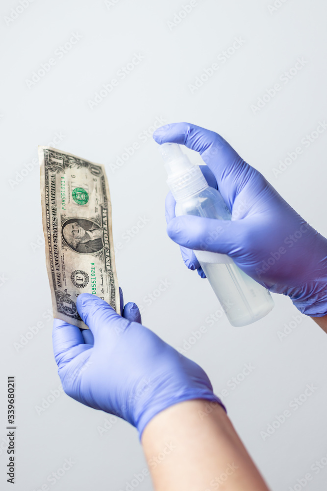 gloved hands disinfecting a US dollar bill with alcohol spray, to ...