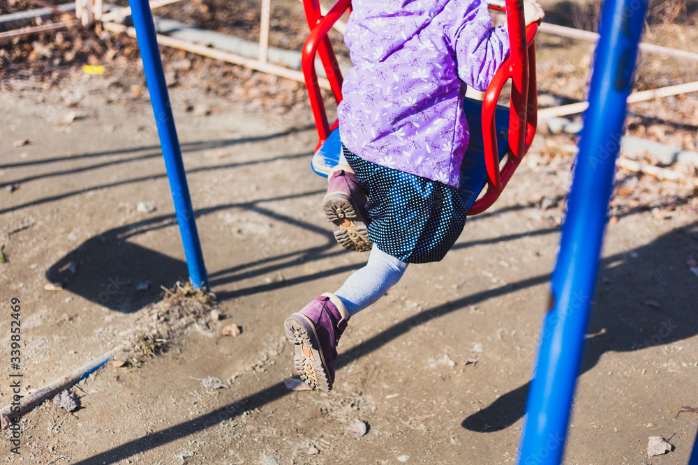 A girl in a hat and jacket walks on the street with her mother, swings ...