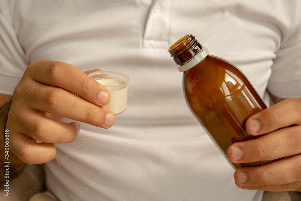 Man in white t-shirt is pouring medical syrup in a measuring cup. Young ...