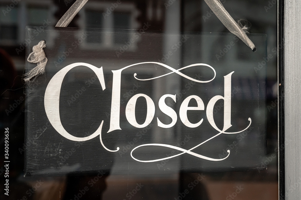 A black and white painted wood closed sign hangs from a ribbon in a ...