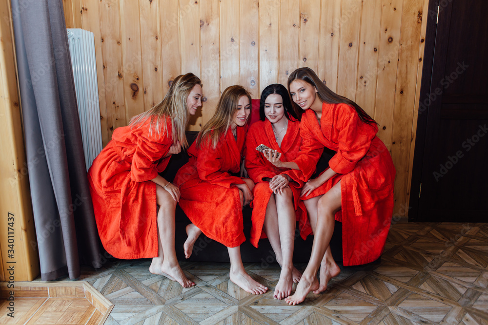Four beautiful young women dressed in red bathrobe sitting on a couch ...