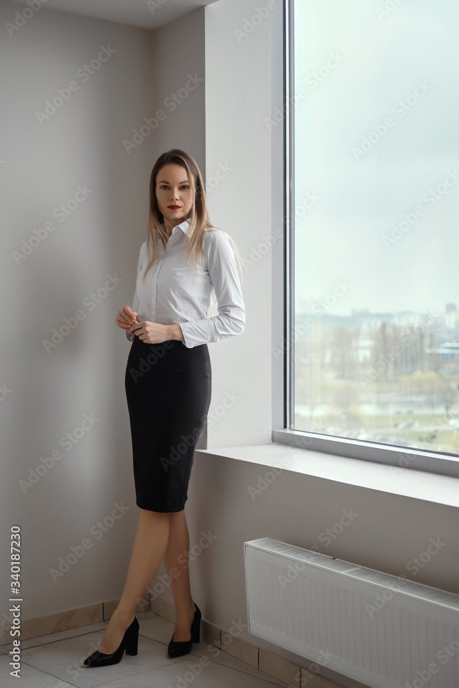 Slim girl in white shirt and black tight skirt posing near the window Stock Photo | Adobe Stock