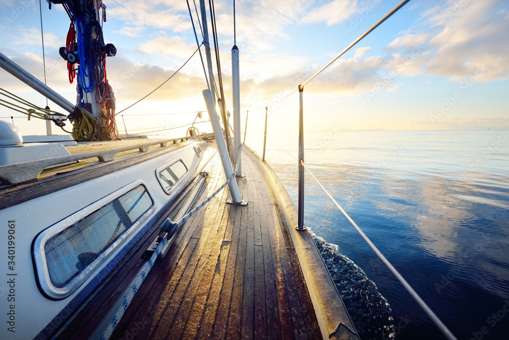 Sloop rigged modern yacht with wooden teak deck sailing at sunrise ...