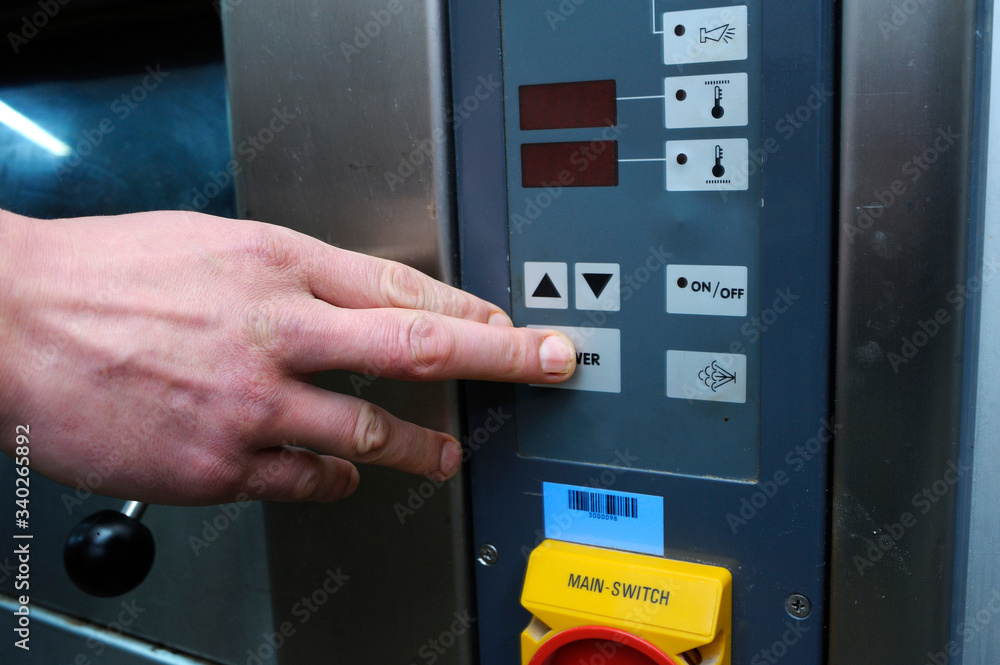At the bakery: baker hand pushing a power button on a control panel of ...