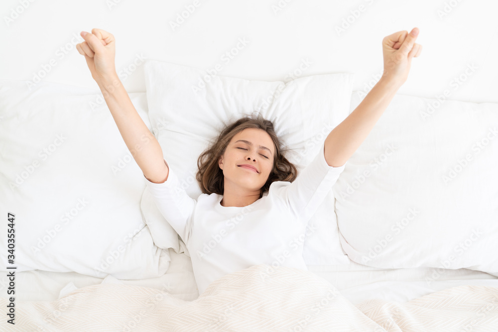 Young girl waking up in morning in white bed and pyjama top, leaving ...