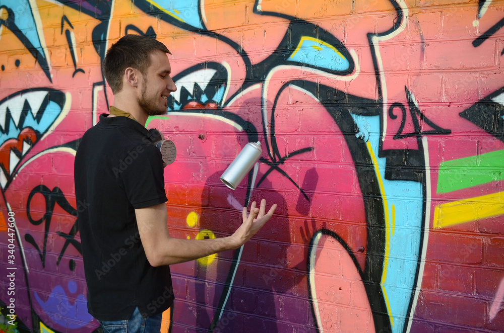 Young graffiti artist with gas mask on his neck throw his spray can ...