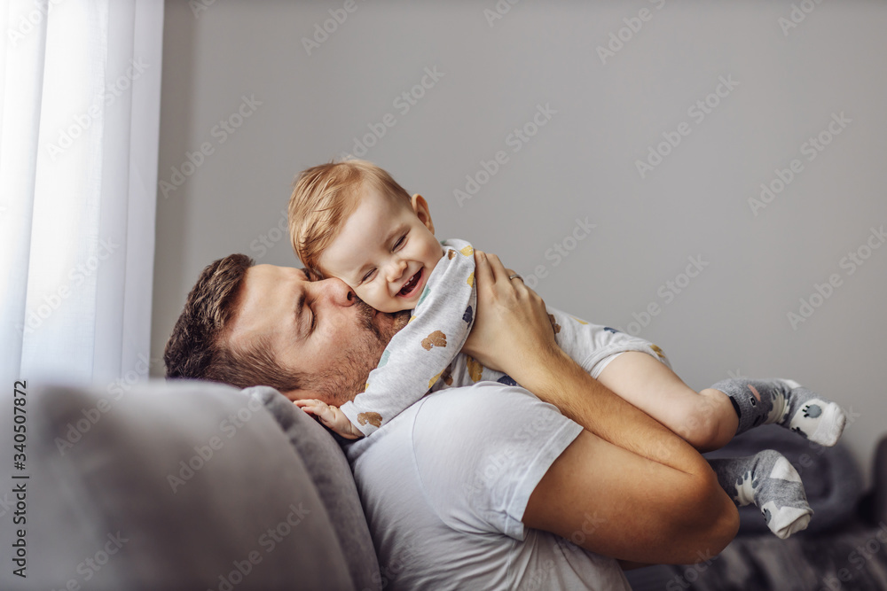 Adorable little blond boy playing with his caring father and biting his ...