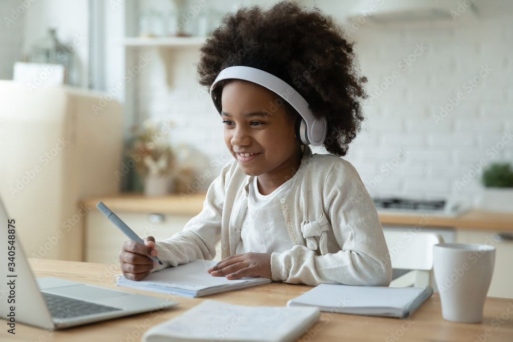 Smiling small African American girl in headphones watch video lesson on ...