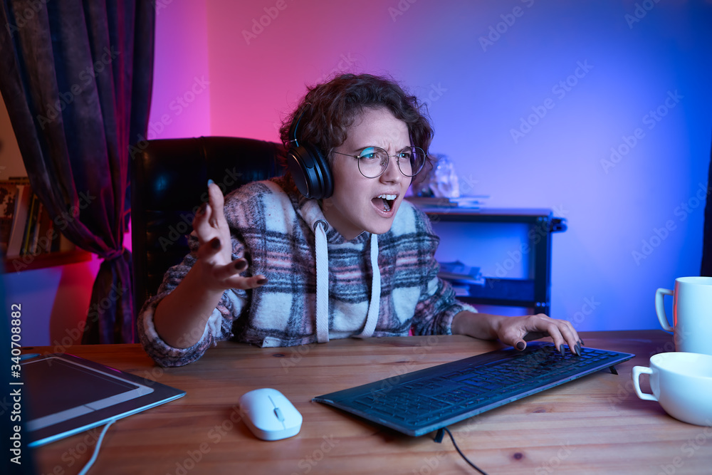 Angry girl looking at the screen of a computer sitting in a cosy chair ...