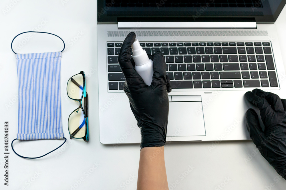 Women's hands in black gloves disinfect a computer with an ...