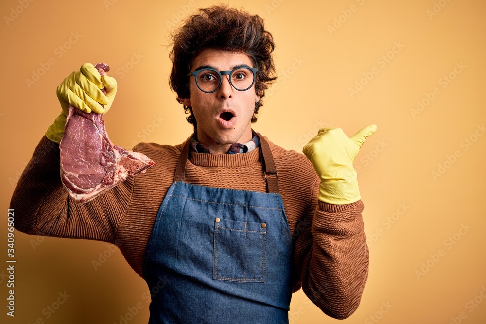 Young handsome butcher man holding meet steak standing over isolated ...