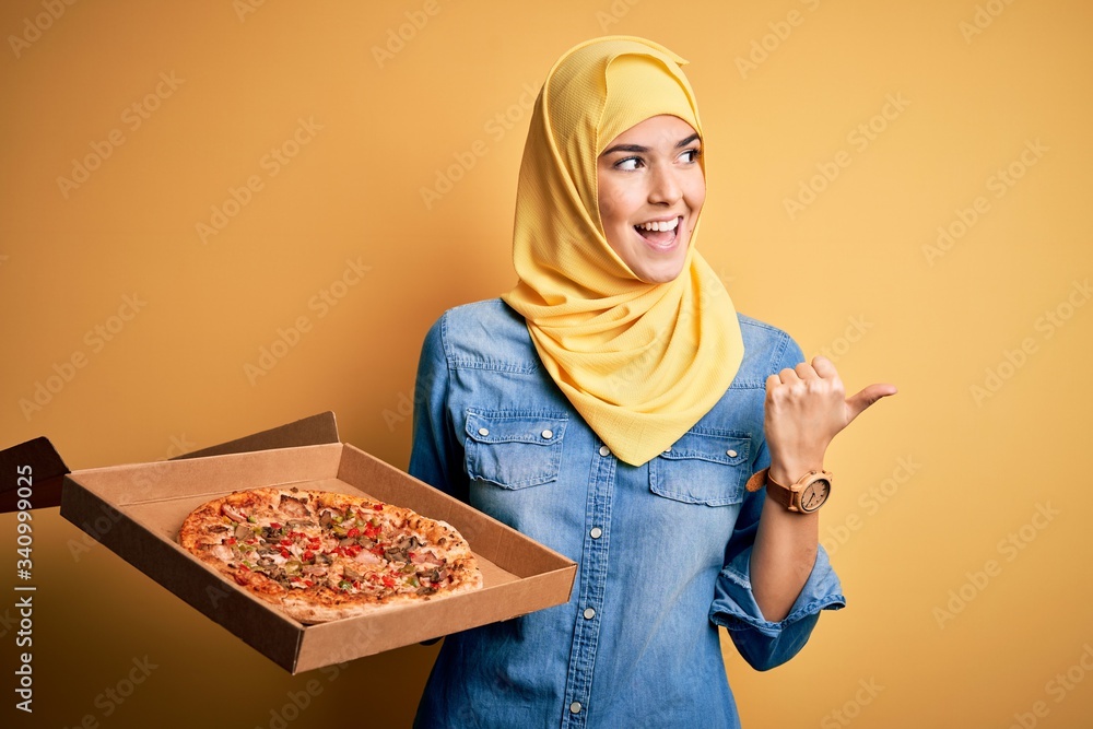 Young girl wearing muslim hijab holding box with Italian pizza over ...