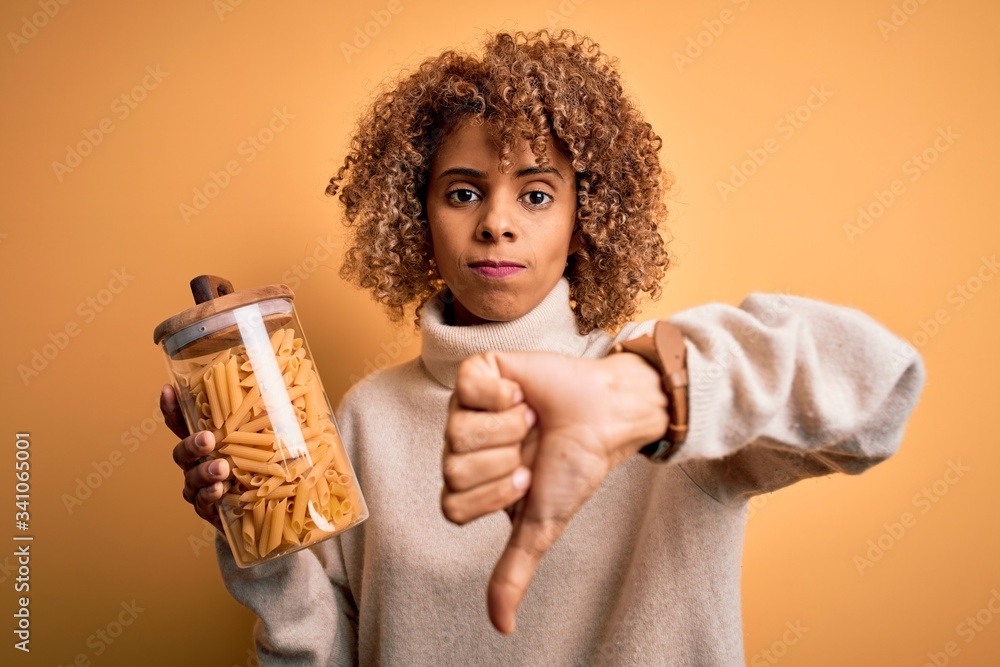 Young african american curly woman holding jar with Italian dry pasta ...