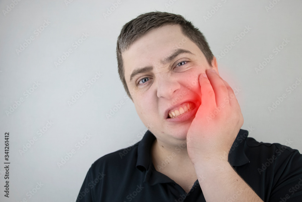 A man clings to his cheek and winces in pain in his tooth. The concept ...