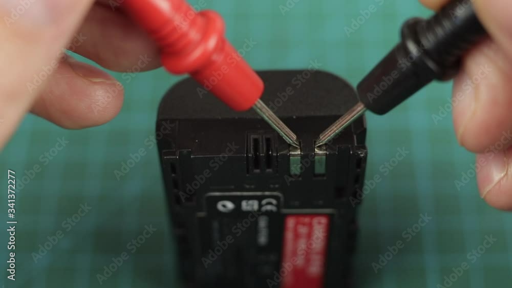 Electronic multimeter tool measuring voltage on lithium battery. Close ...